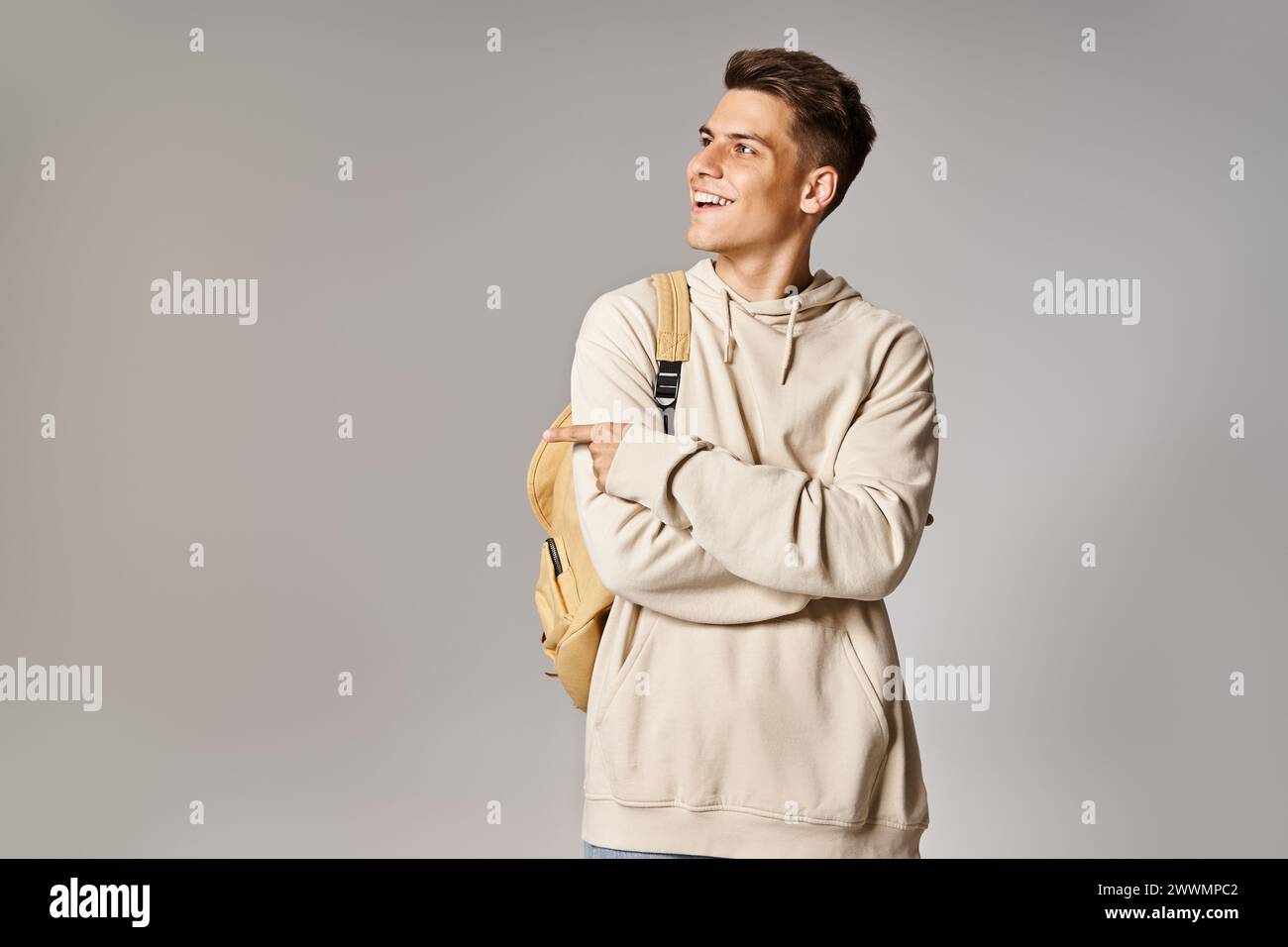 attractive young man with backpack and folded arms showing side with ...