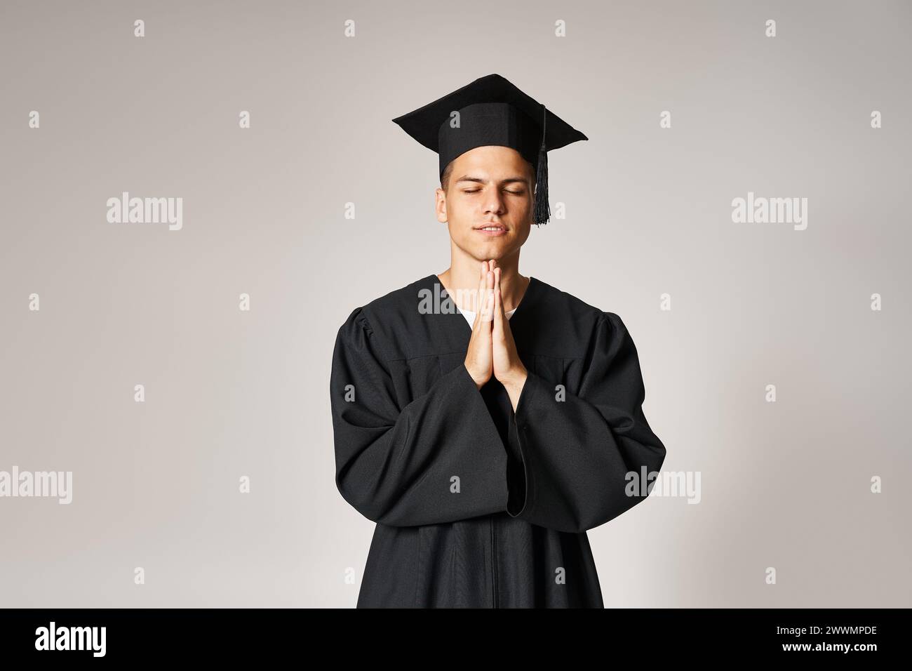 portrait of hopeful young student in graduate gown and cap with folded ...