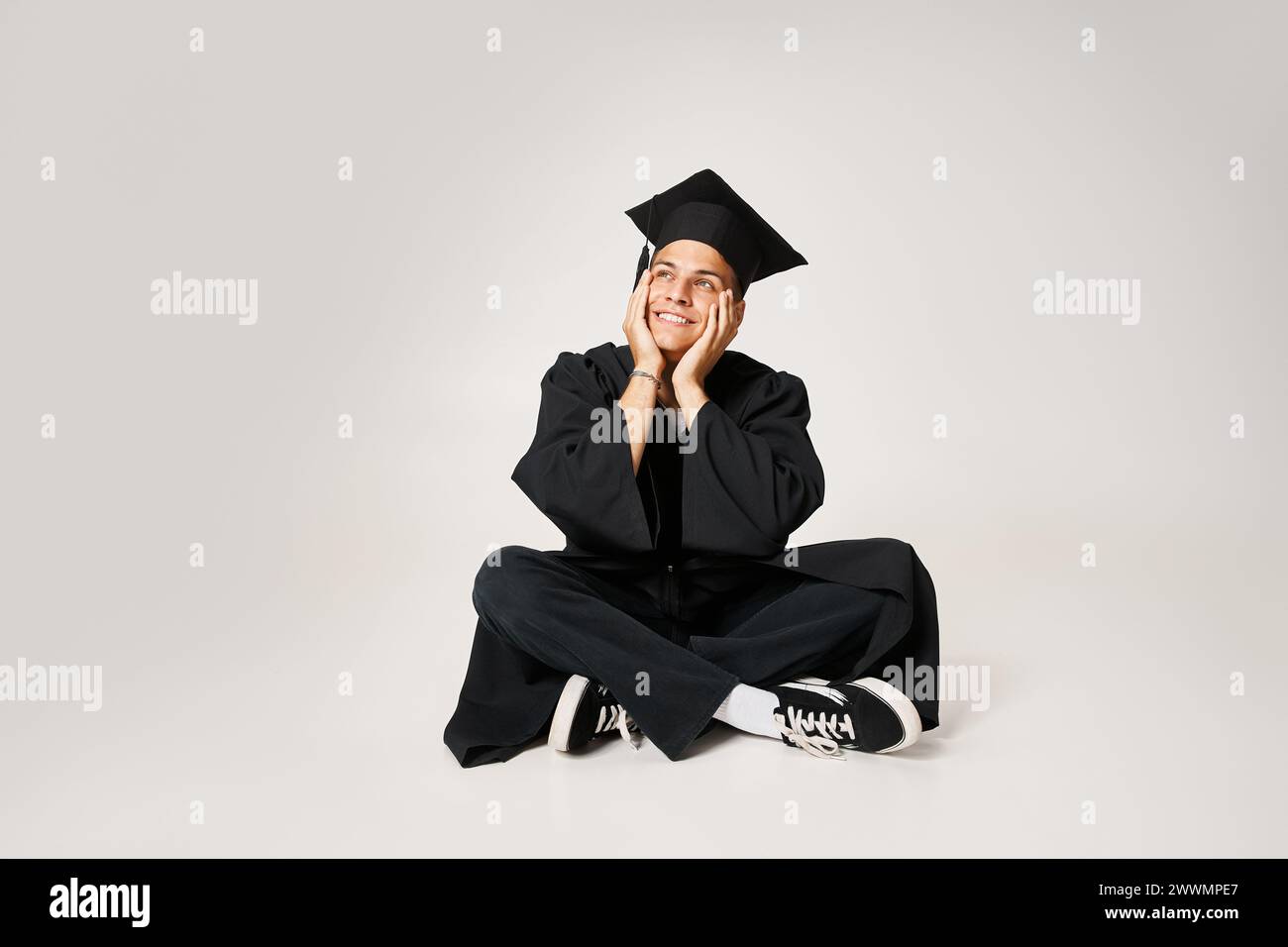 smiling charming guy in graduate outfit sitting and holding with hands ...