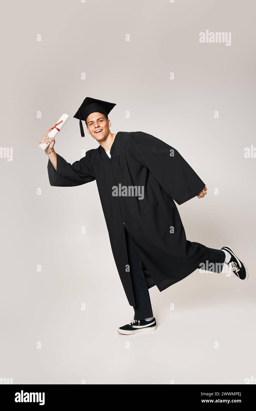 playful young man in graduate outfit posing with diploma in hand on ...