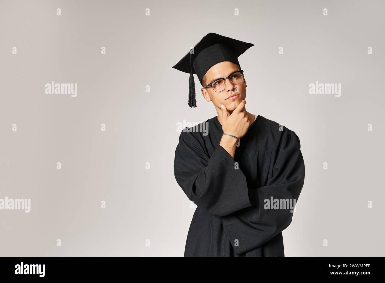 thoughtful guy in graduate outfit and vision glasses touching hand to ...