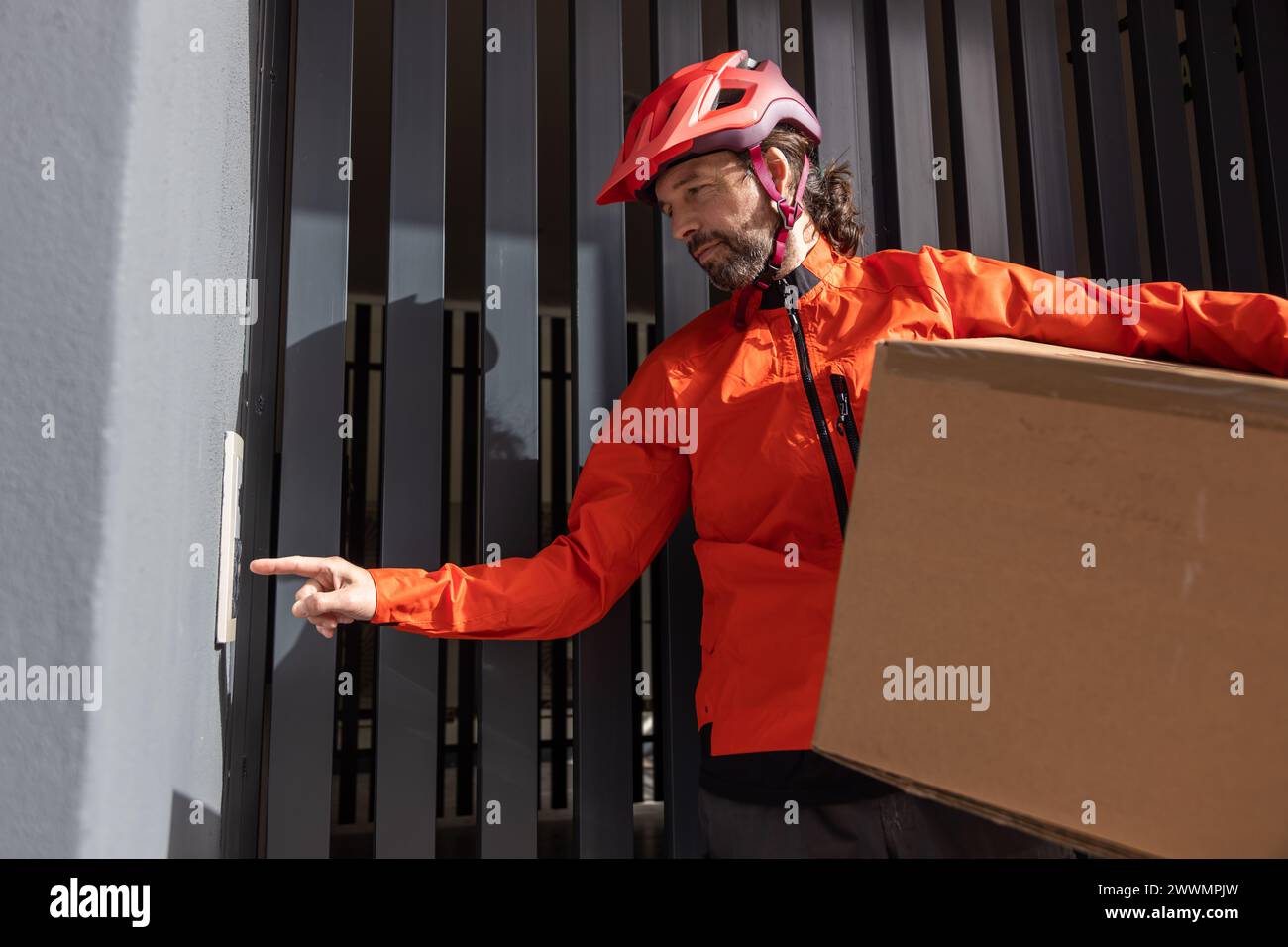 young courier with red clothing and helmet riding cargo bike arriving at the shipping ...