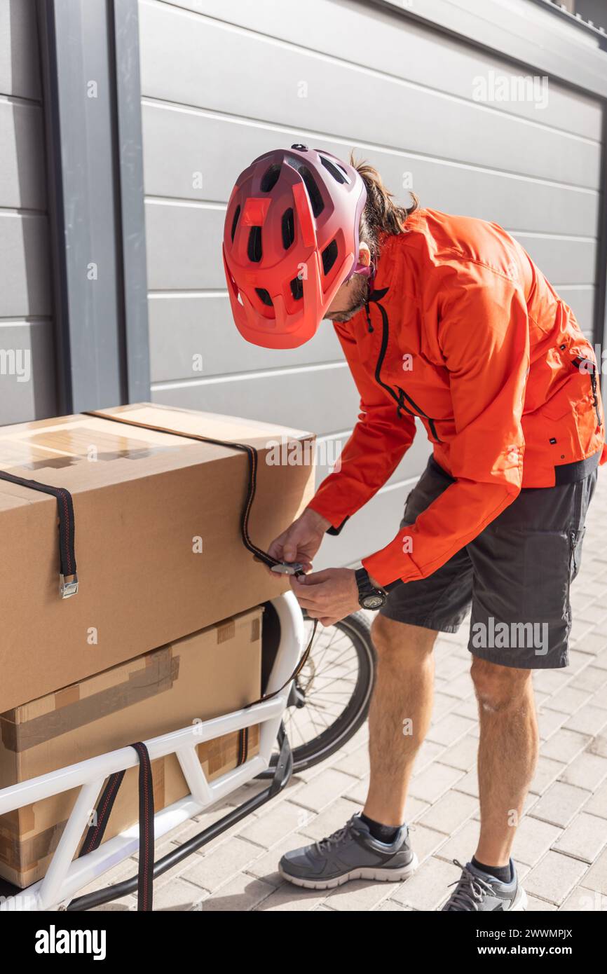 young courier with red clothing and helmet riding cargo bike arriving ...