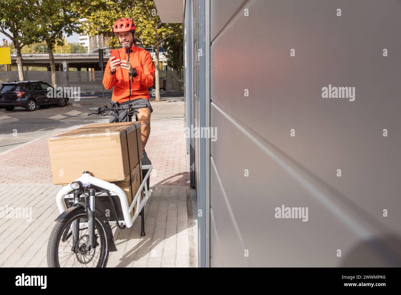 young courier with red clothing and helmet riding cargo bike arriving ...