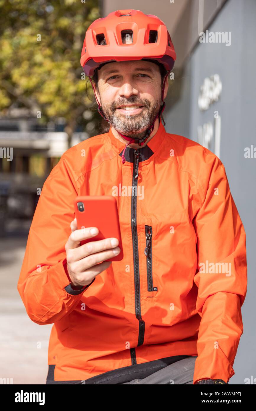 young courier with red clothing and helmet riding cargo bike arriving at the shipping ...