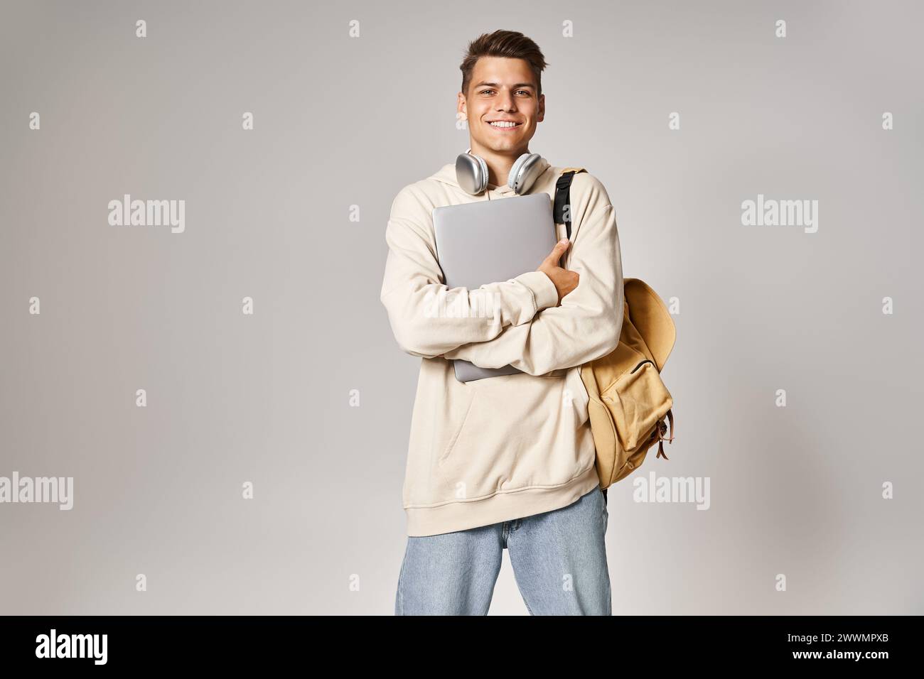 cheerful student in 20s with laptop and headphones confident standing ...