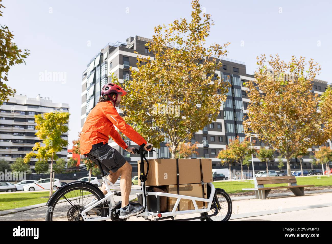 young courier with red clothing and helmet riding cargo bike , riding ...