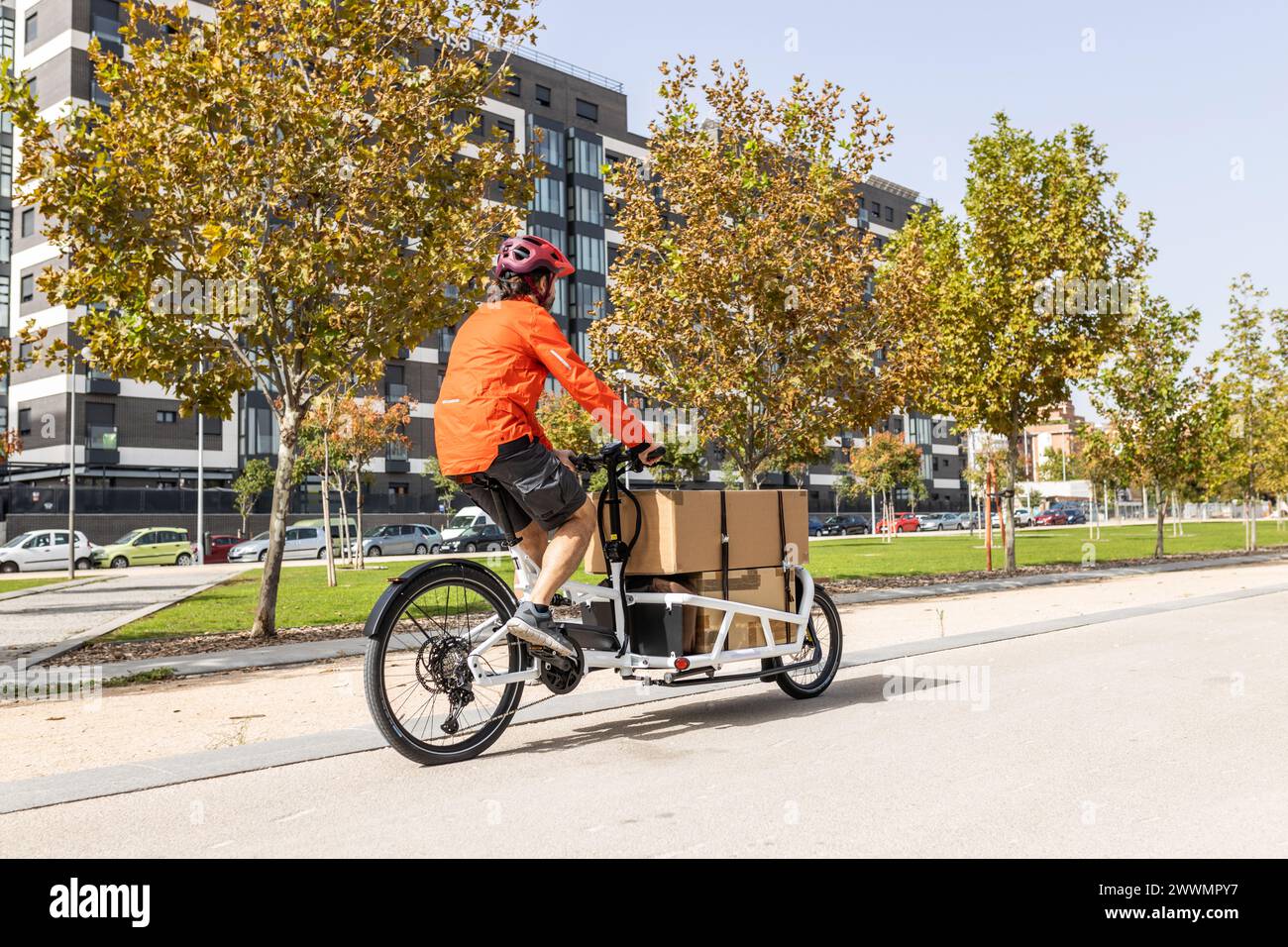 young courier with red clothing and helmet riding cargo bike , riding ...