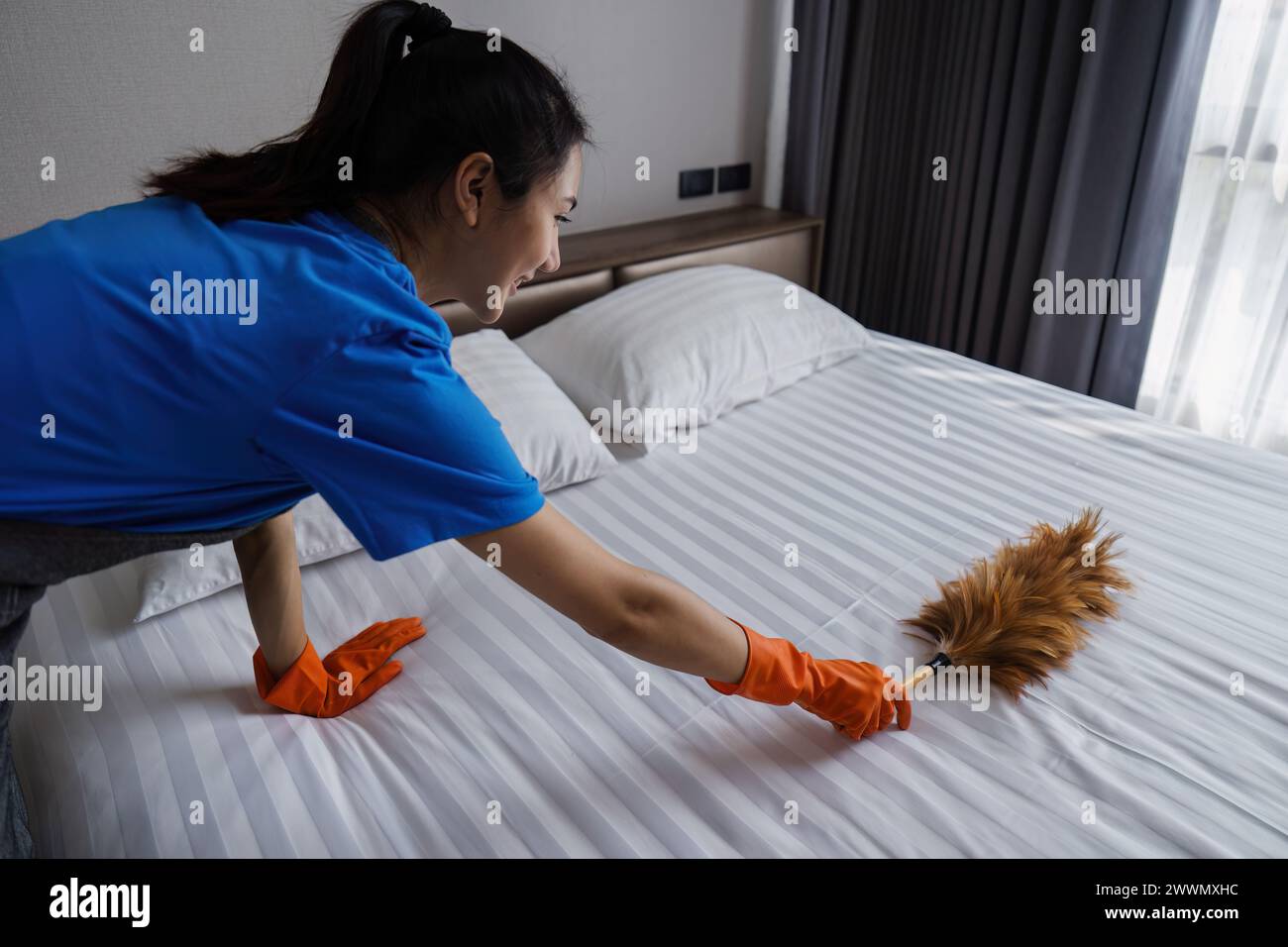 cleaning service woman cleaning dust on bed with feather duster. housekeeping cleaning service ...