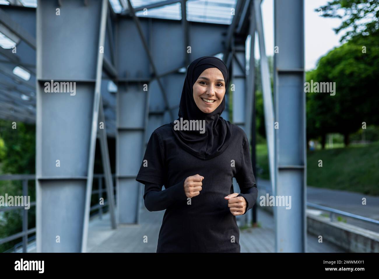 An active woman in hijab running on a city bridge, depicting health ...