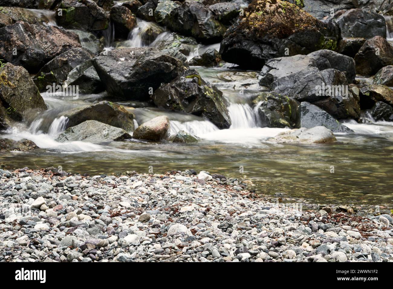 A stream running over lichen covered rocks and boulders creating small ...