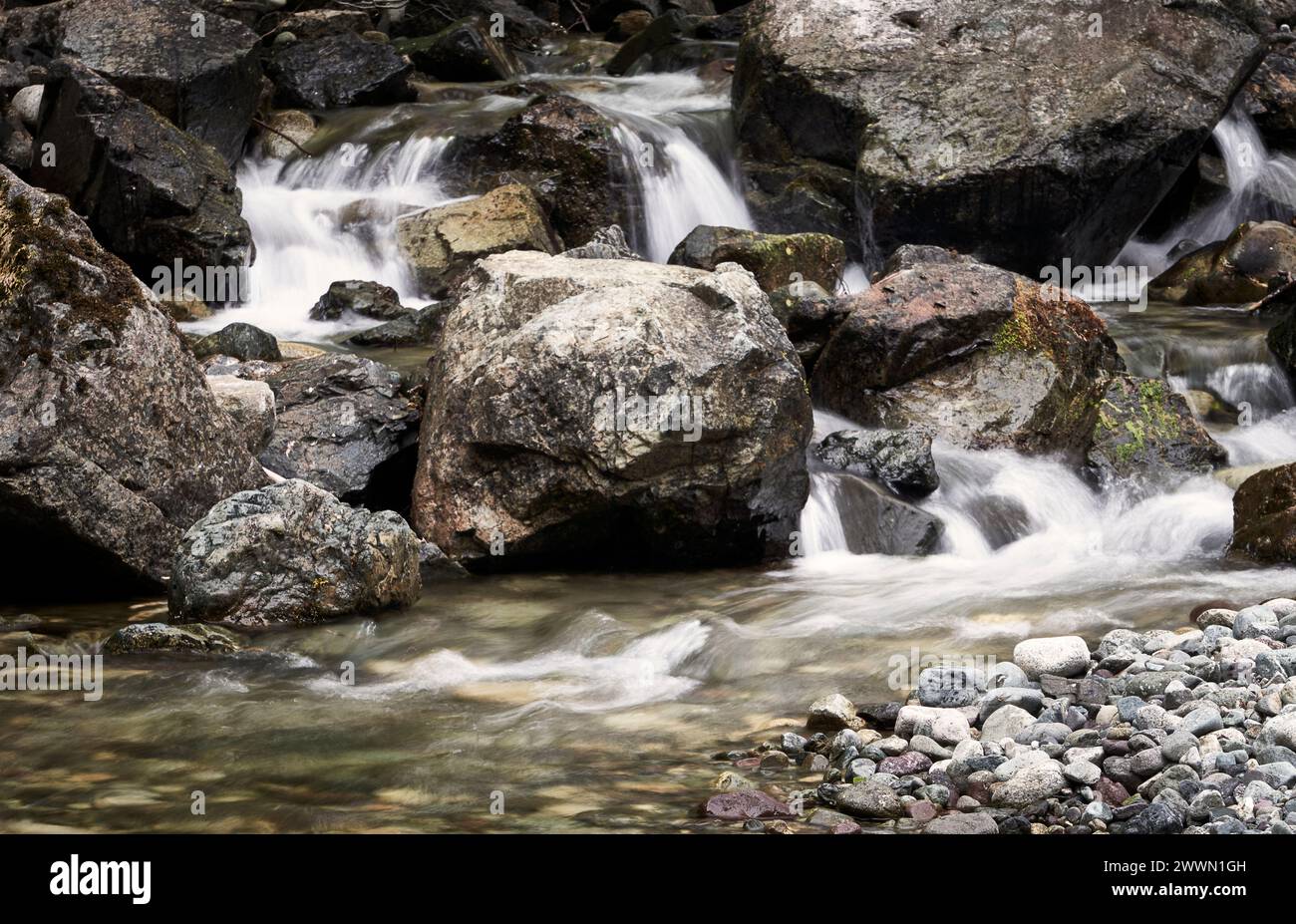 Water in a creek bed rushing over boulders and rocks and forming little ...