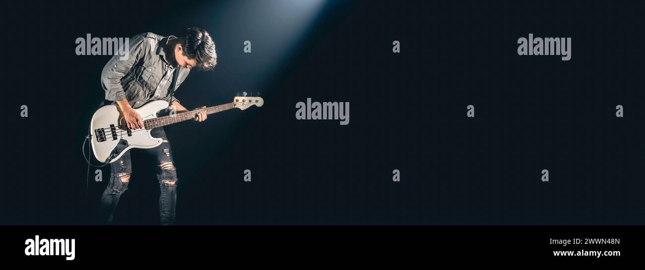 A male guitarist plays an electric guitar on a dark stage background ...