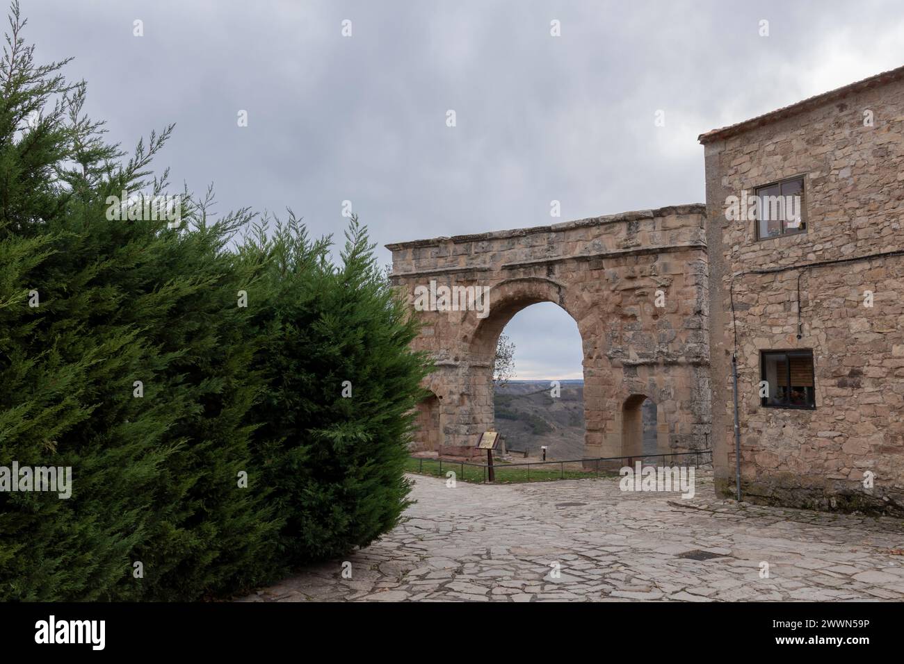 old stone building with a large archway, adjacent to a green bush ...
