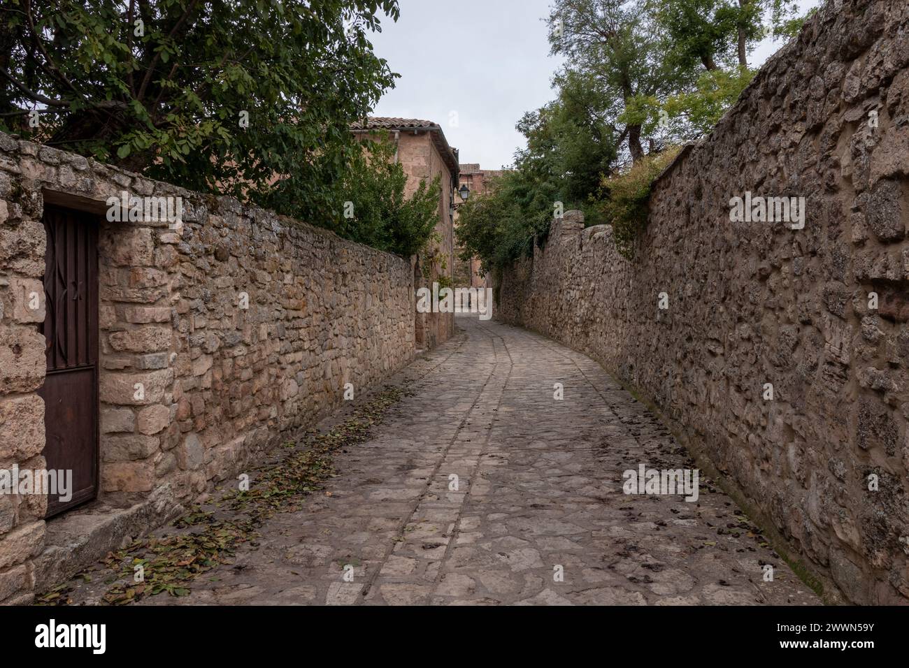 narrow, stone-paved street flanked by old, textured stone walls ...