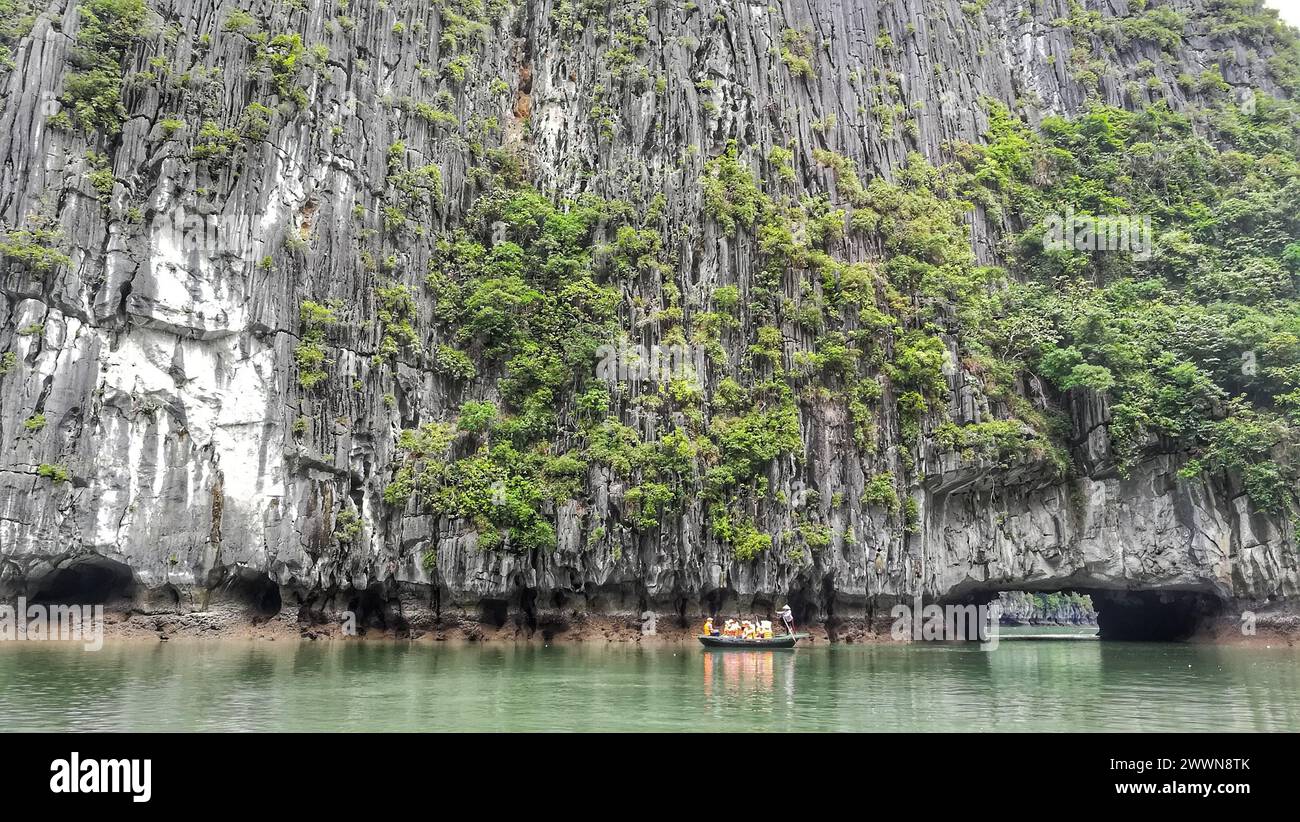 A group of people in a boat sailing by majestic cliffs. Halong Bay ...