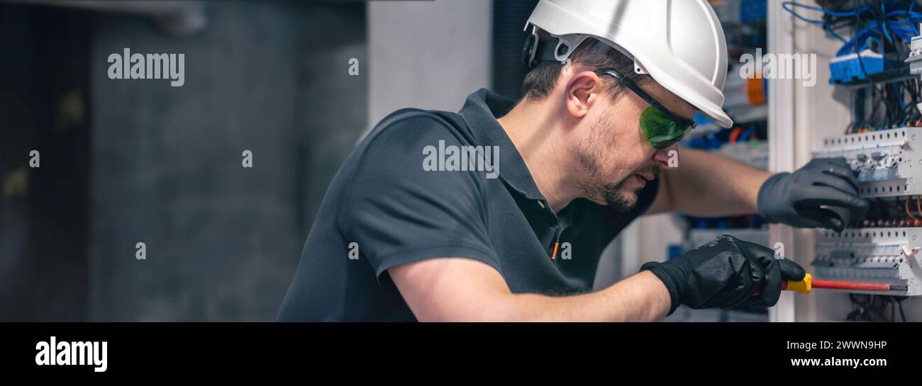 A male electrician works in a switchboard using an electrical ...
