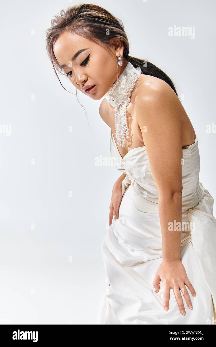 charming asian girl in elegant white dress leaning forward and looking ...