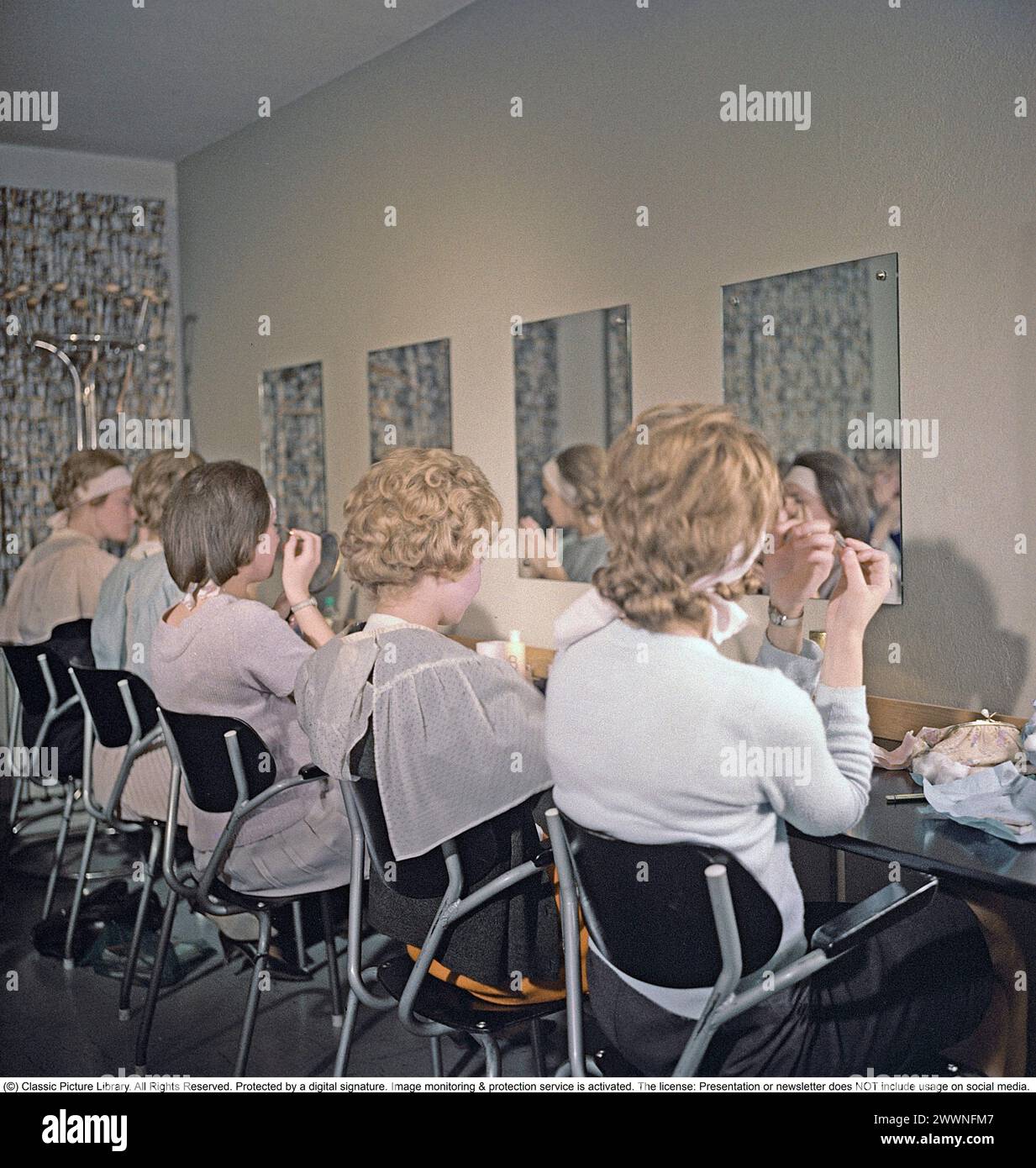 In the 1960s. A group of women are sitting in front of mirrors applying ...
