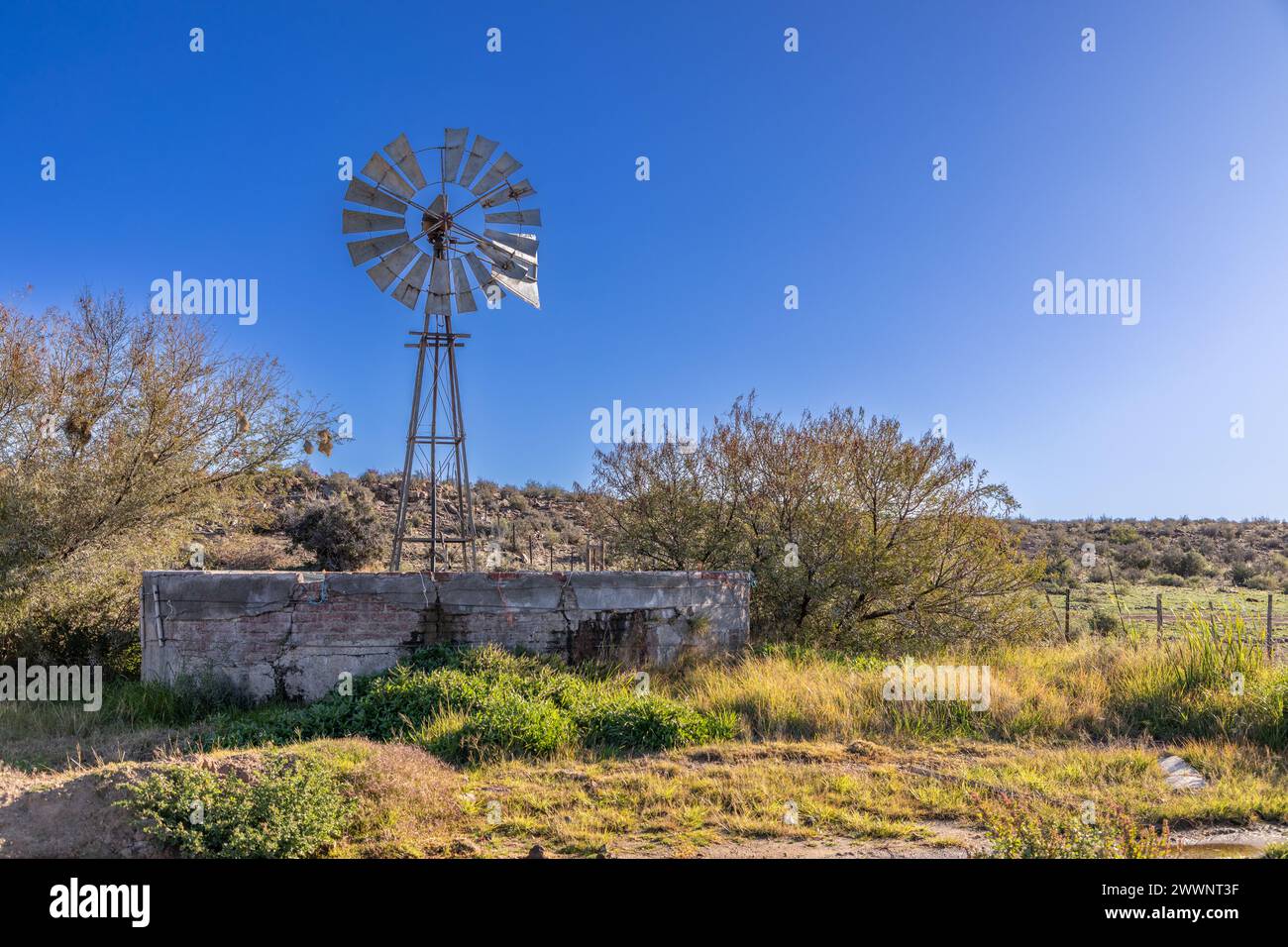 Old and unused metal windmill and dilapidated brick and concrete dam in ...