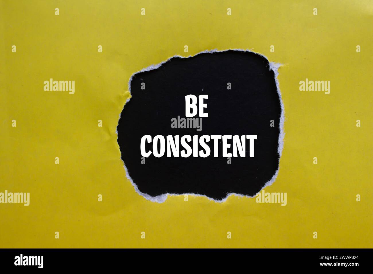 Be consistent words written on yellow torn paper with black background ...