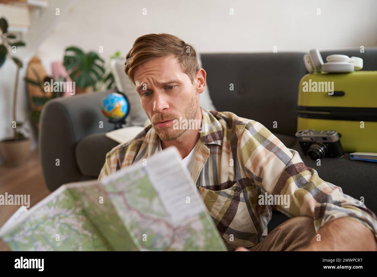 Portrait of confused guy looking at travel map, choosing route, going ...