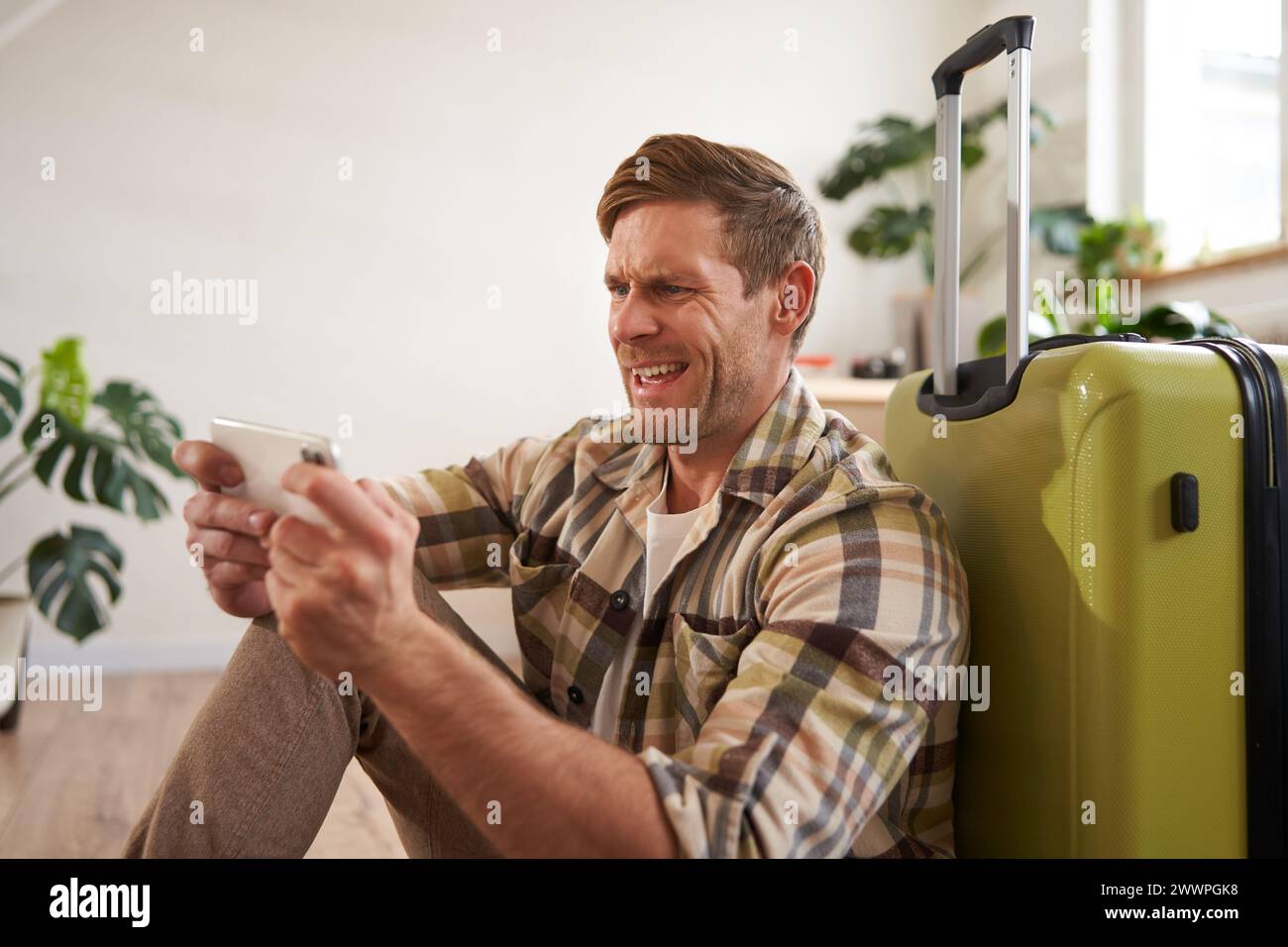 Man with shocked face, sitting on floor with suitcase, looking worried ...