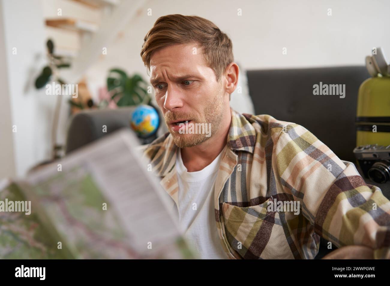 Portrait of confused guy looking at travel map, choosing route, going ...