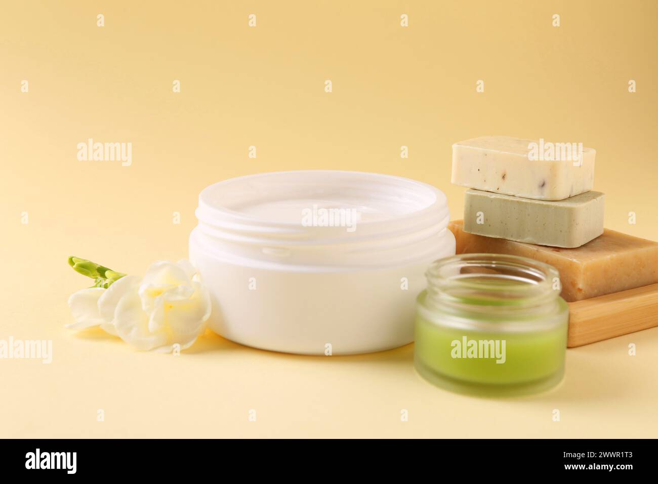 Moisturizing cream in open jars, soap bars and freesia flower on beige ...