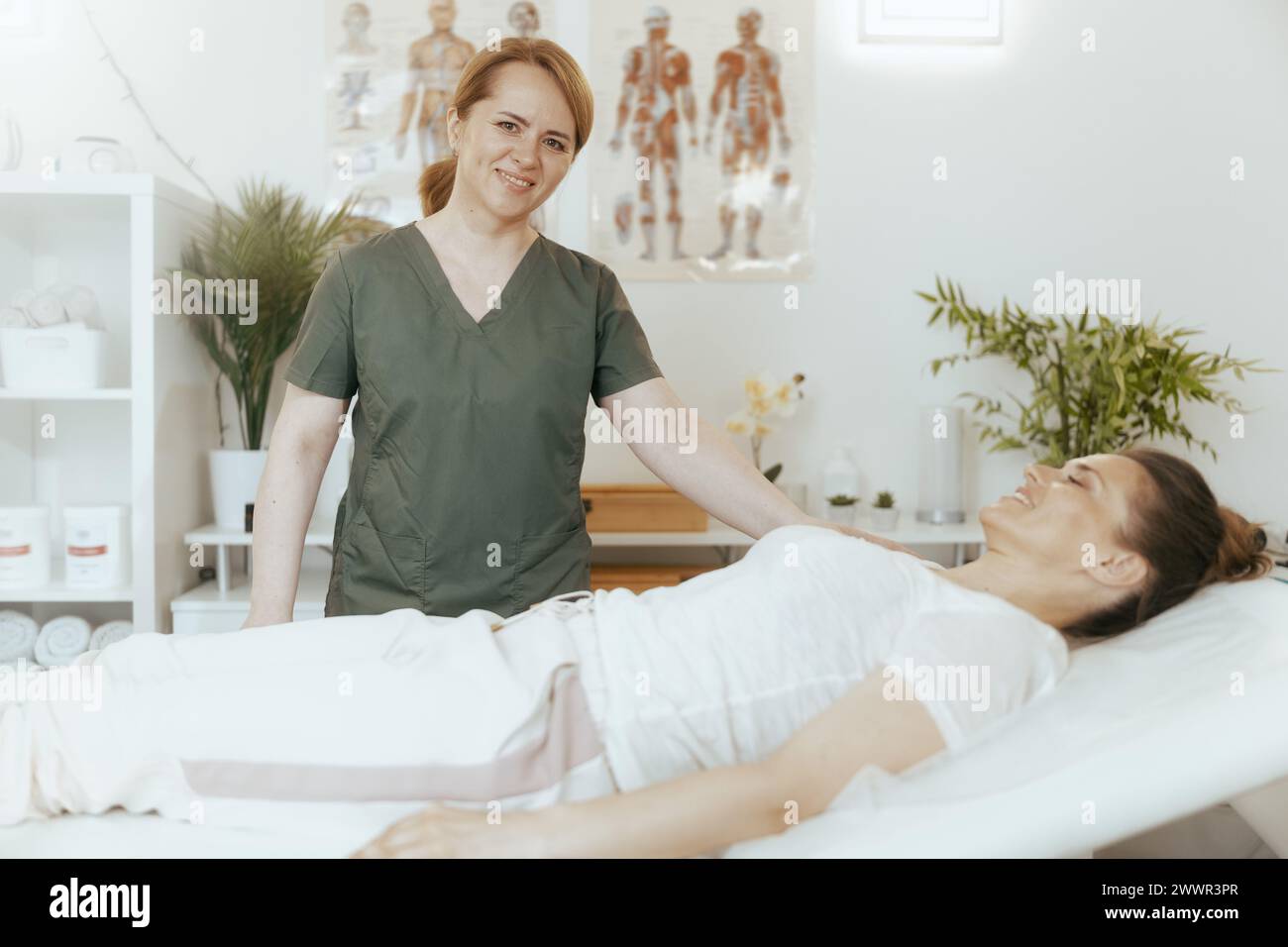 Healthcare time. smiling massage therapist woman in massage cabinet with client doing checkup ...