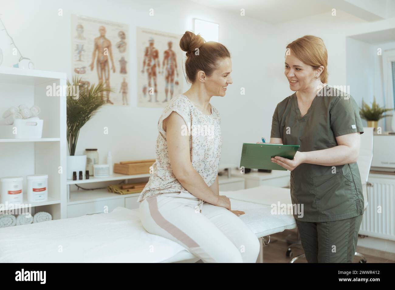 Healthcare time. smiling female massage therapist in massage cabinet with client conducting ...