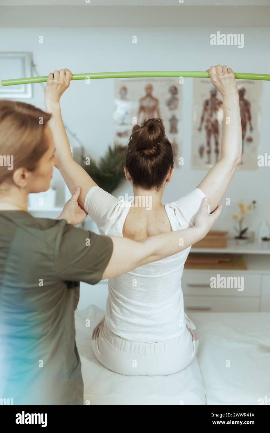 Healthcare time. Seen from behind female medical massage therapist in massage cabinet with ...