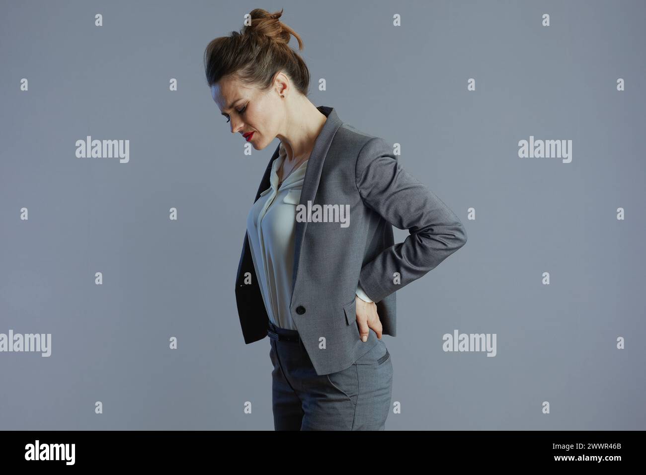 tired elegant 40 years old woman employee in grey suit having back pain ...