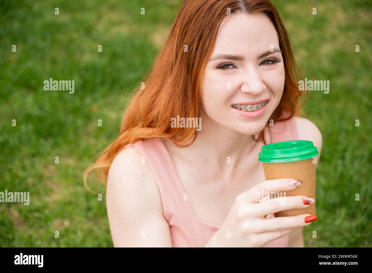 Beautiful young woman with braces on her teeth drinks from a cardboard ...