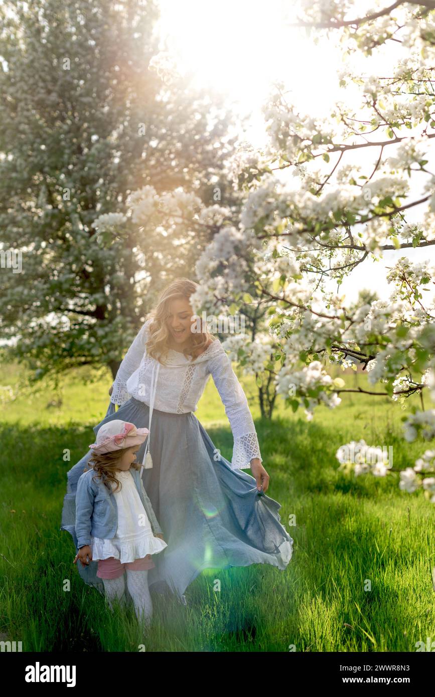 A little girl and her mother are walking in the meadow under a blooming ...