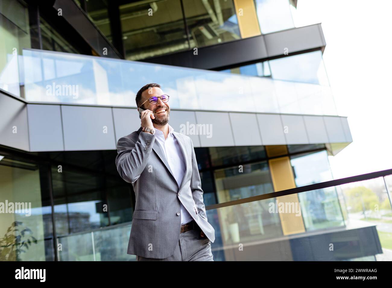 Suited man with arms crossed stands proudly before a sleek building ...