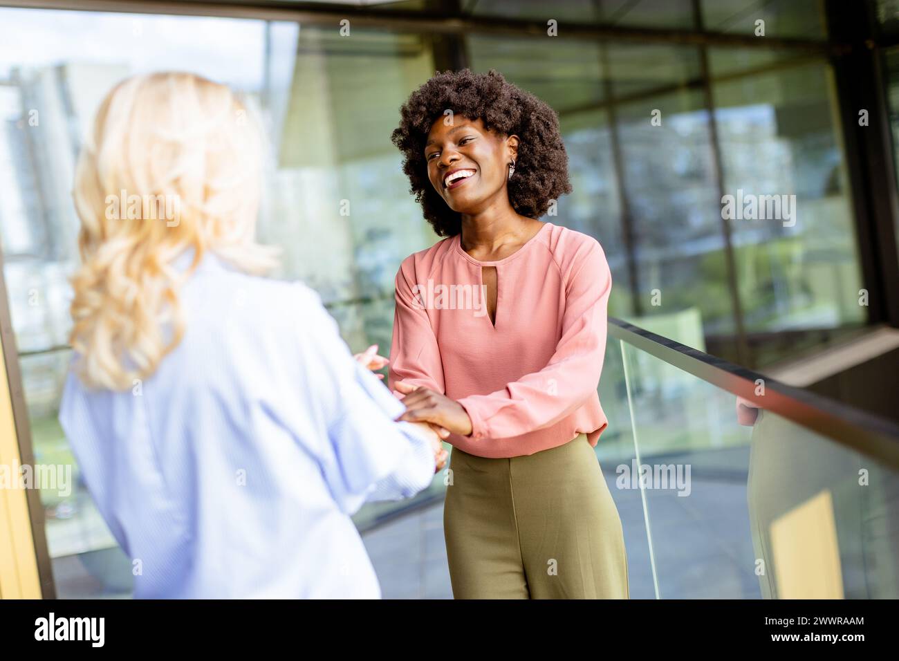 Two women engage in a friendly handshake, one laughing joyously ...