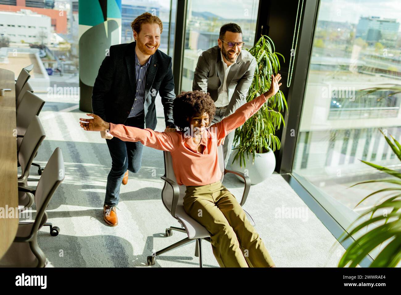 Exuberant co-workers engage in an impromptu office chair race, basking ...