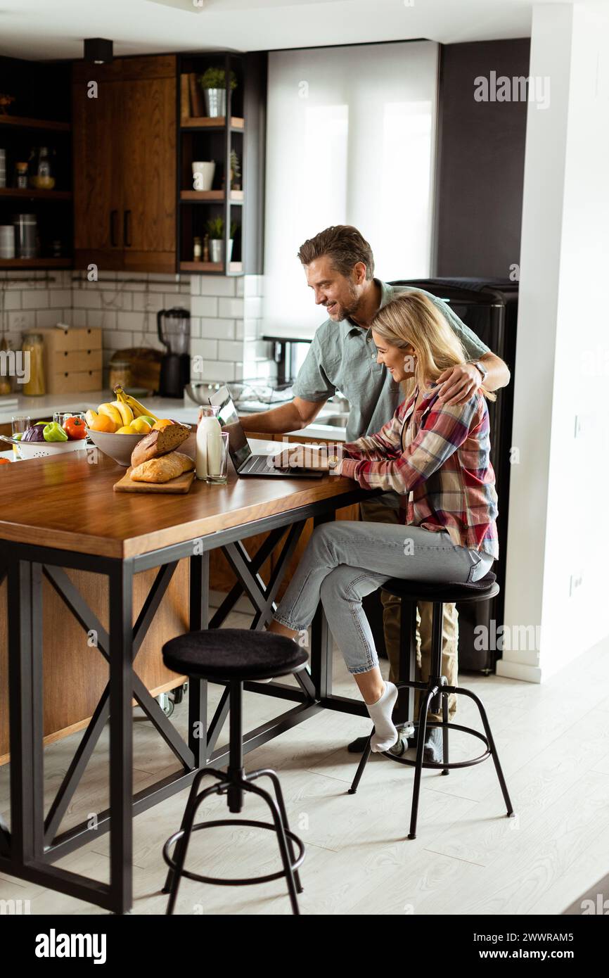 A cheerful couple enjoys a light-hearted moment in their sunny kitchen ...