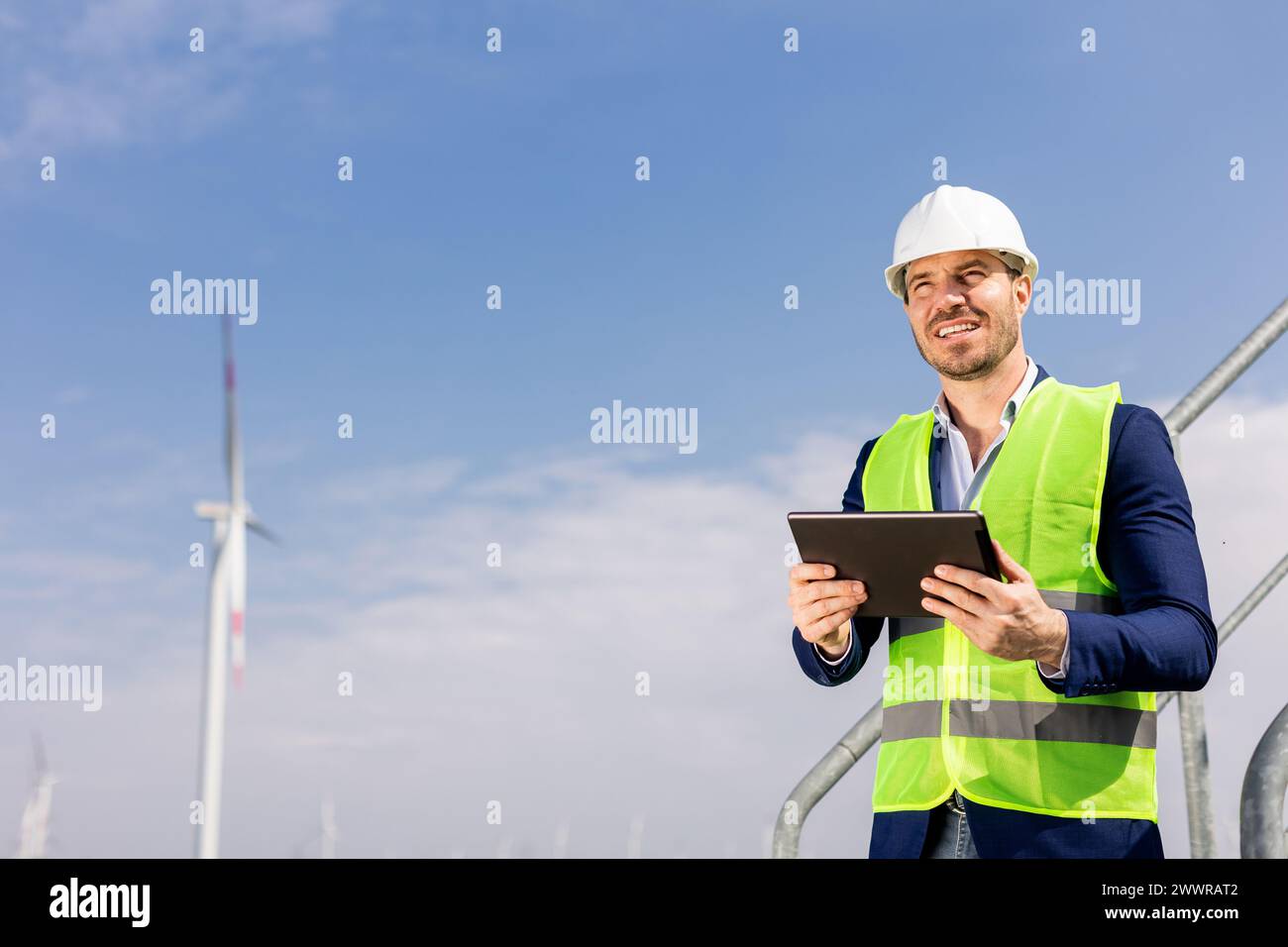A cheerful engineer in safety gear reviews data on a tablet before ...