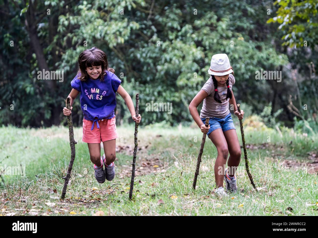 Summer joy as kids race in a natural setting, sticks in hand and ...