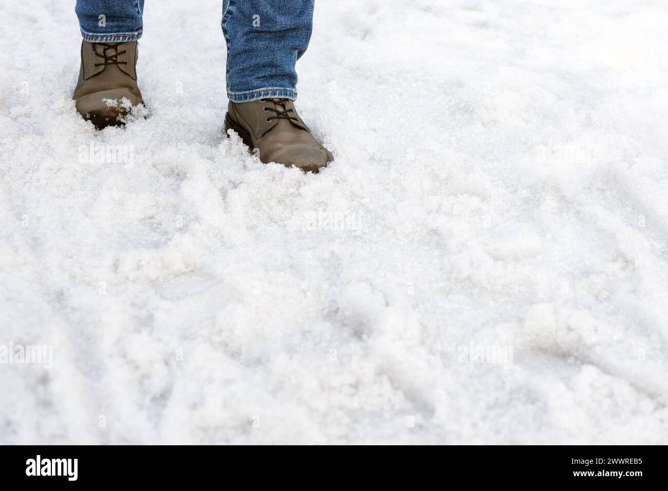 a man in boots walks through melted snow. man walks on loose snow ...