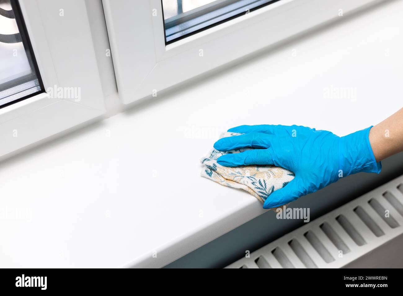 housewife wearing gloves wipes a plastic window sill. a hand in a blue ...