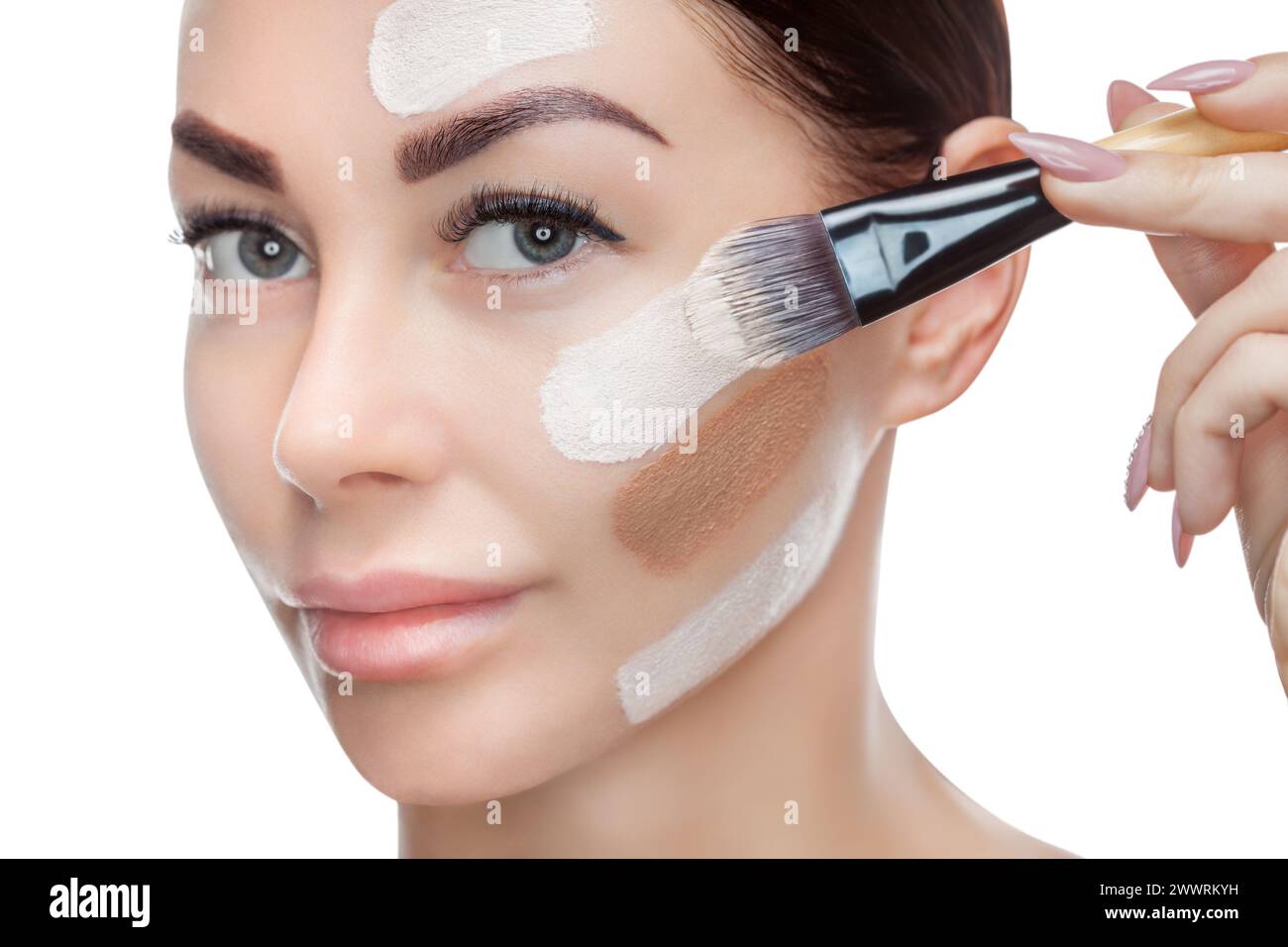 Beautiful young woman is applying a foundation on her face with a brush ...