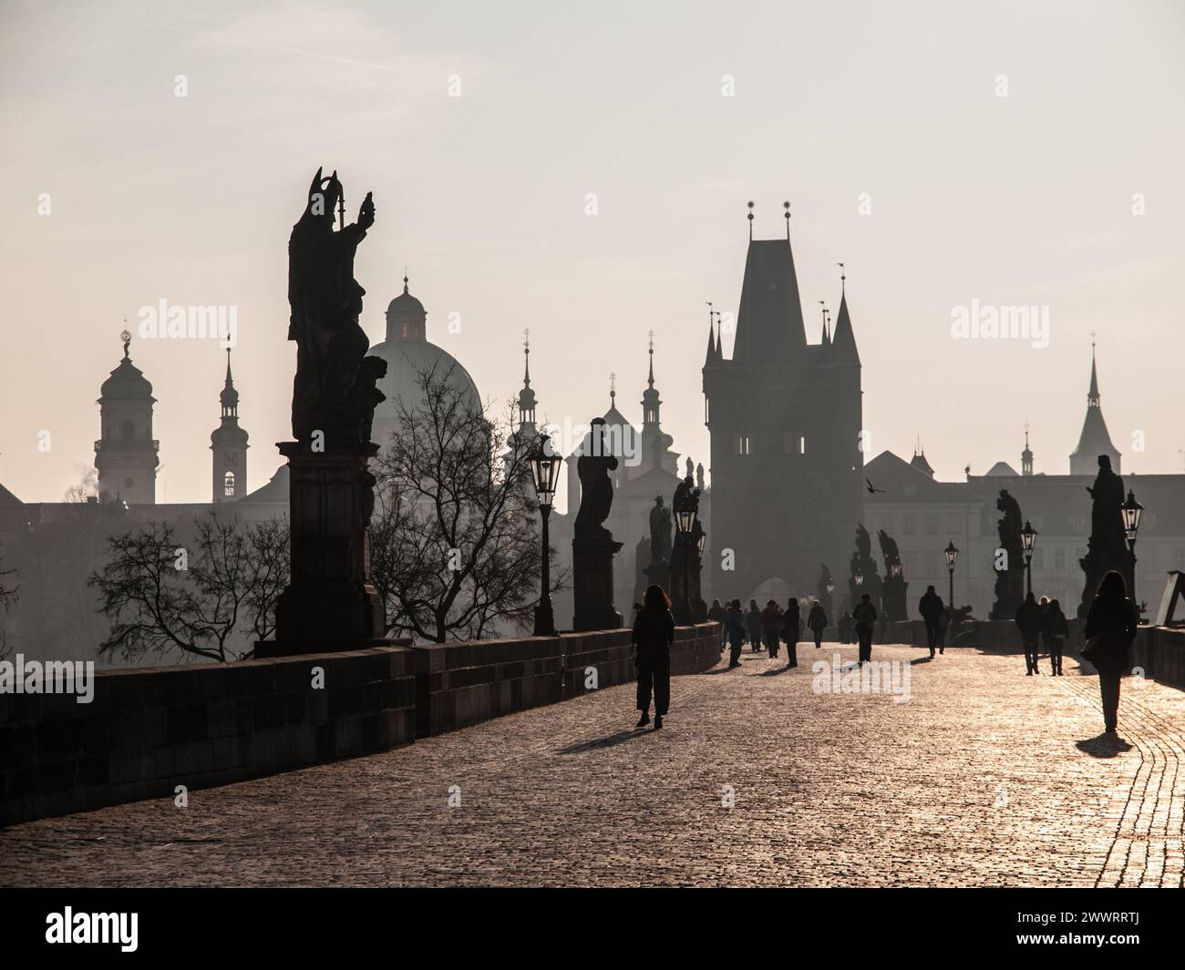 Tourists walk on Charles Bridge on sunny morning under silhouettes of ...
