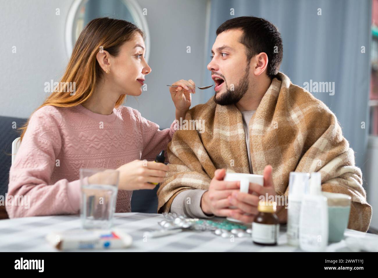 Man with cold symptoms sitting at home while girlfriend caring him ...