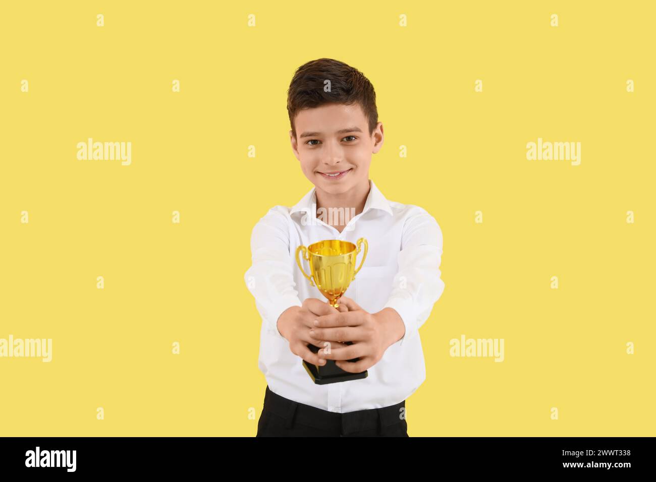 Smart little school boy with prize cup on yellow background Stock Photo ...