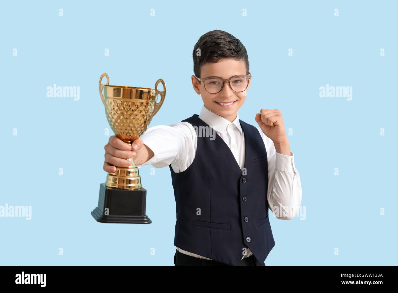 Smart little school boy with prize cup on light blue background Stock ...
