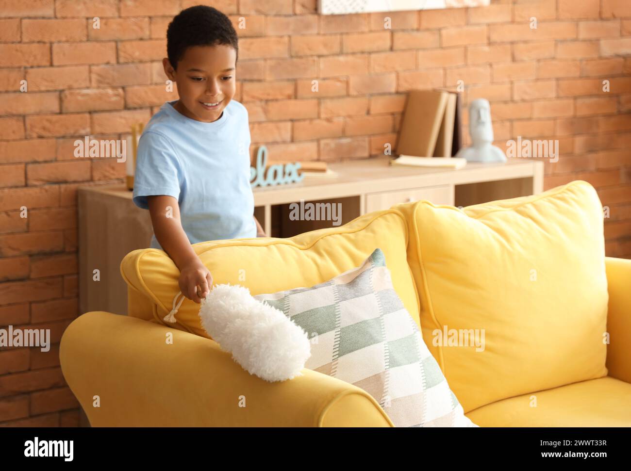 Cute little African-American boy cleaning sofa with duster in living ...