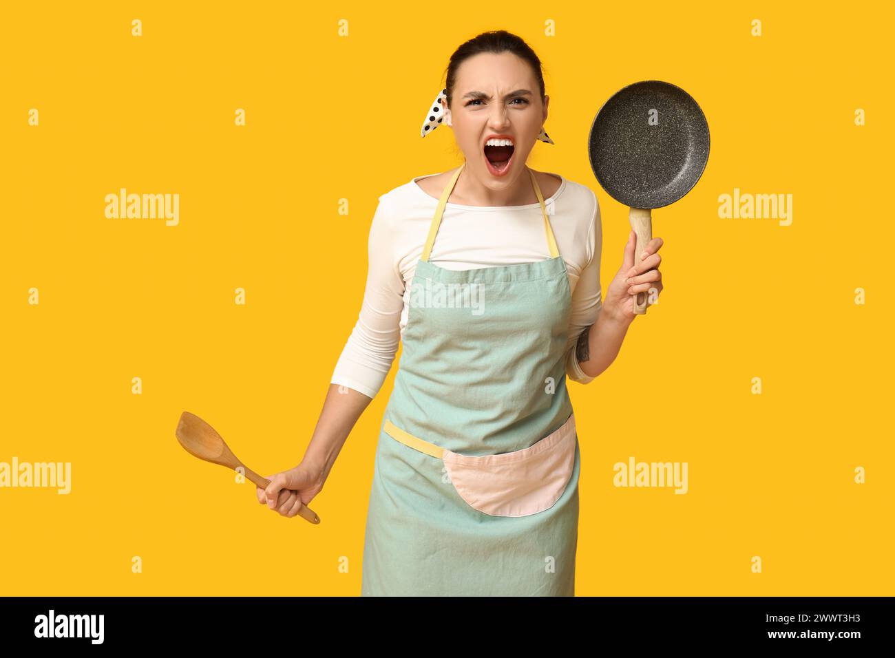 Portrait of angry young housewife in apron with frying pan and wooden ...